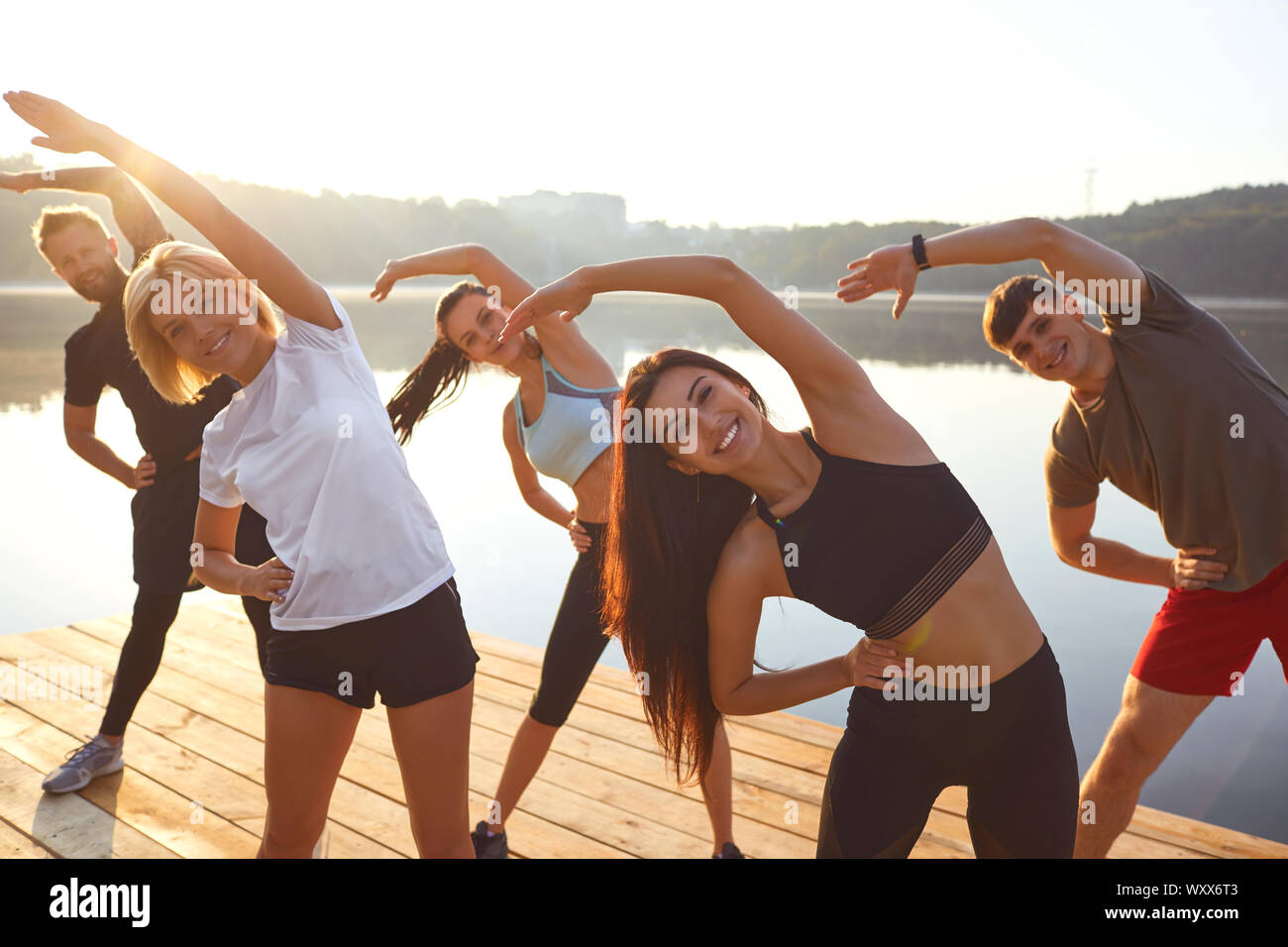 A group of active people do exercises in the park near the lake Stock ...