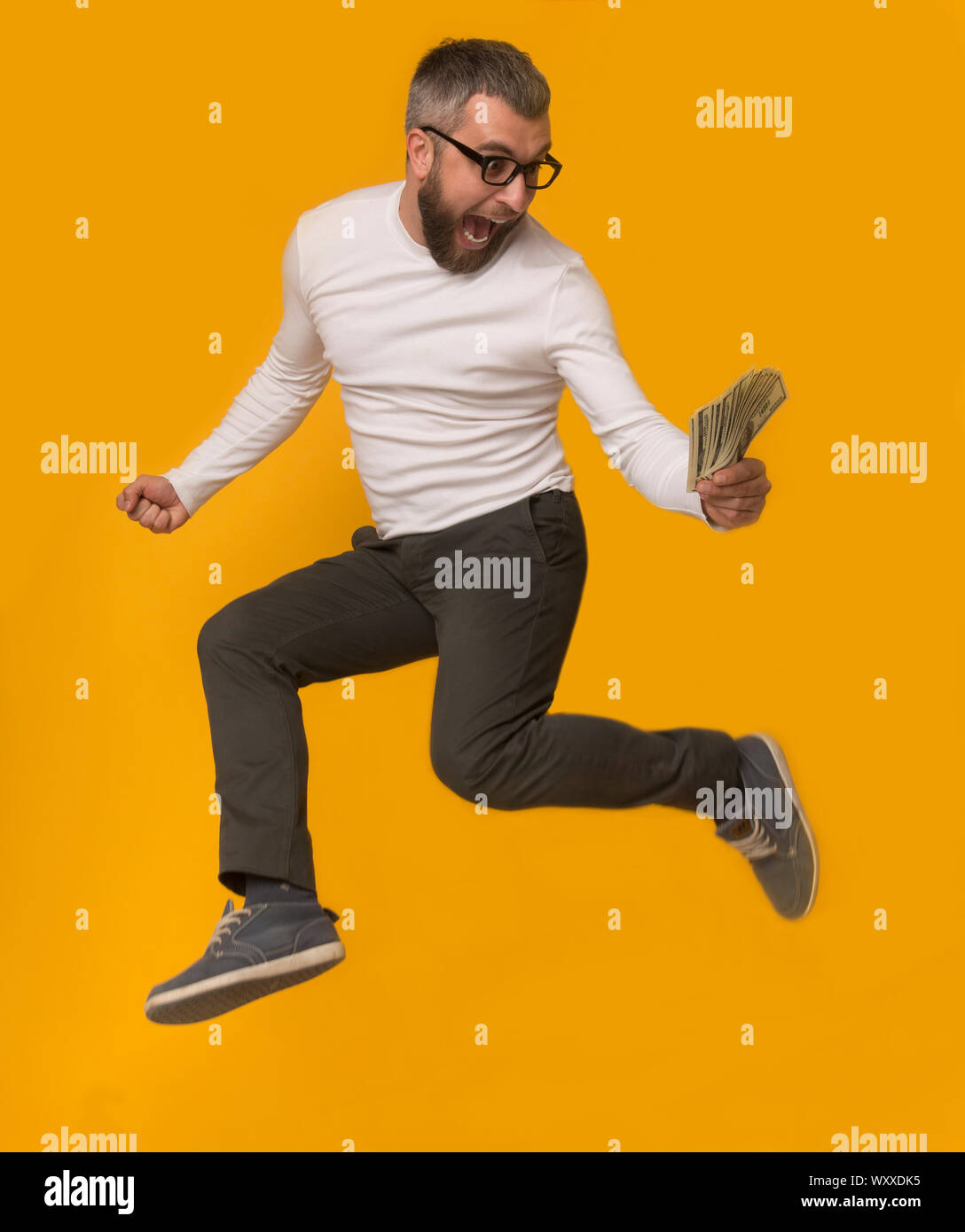 Excited man jumping with money on yellow background Stock Photo - Alamy