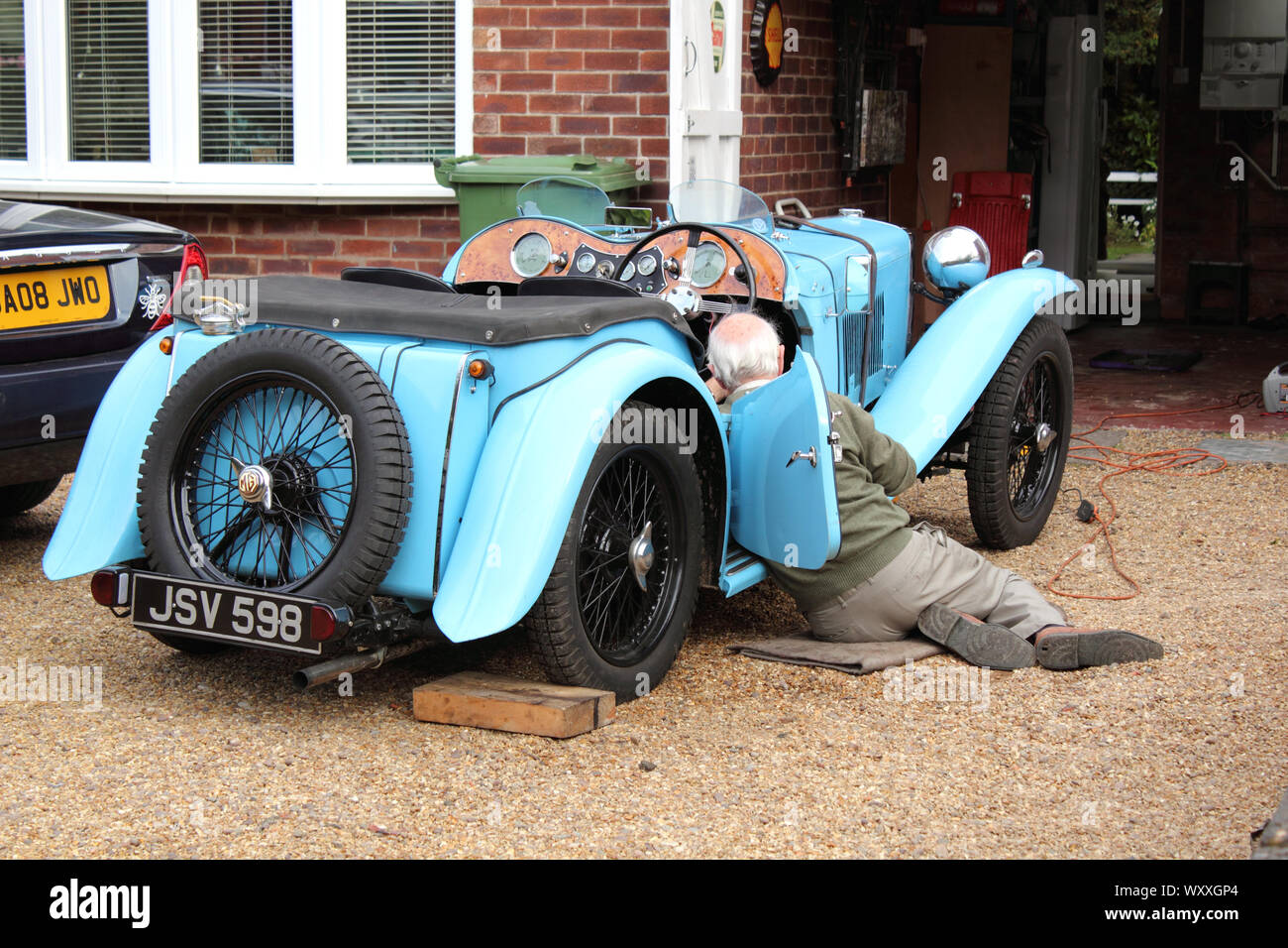 View of elderly man working on blue vintage Morgan car from the 1930s ...