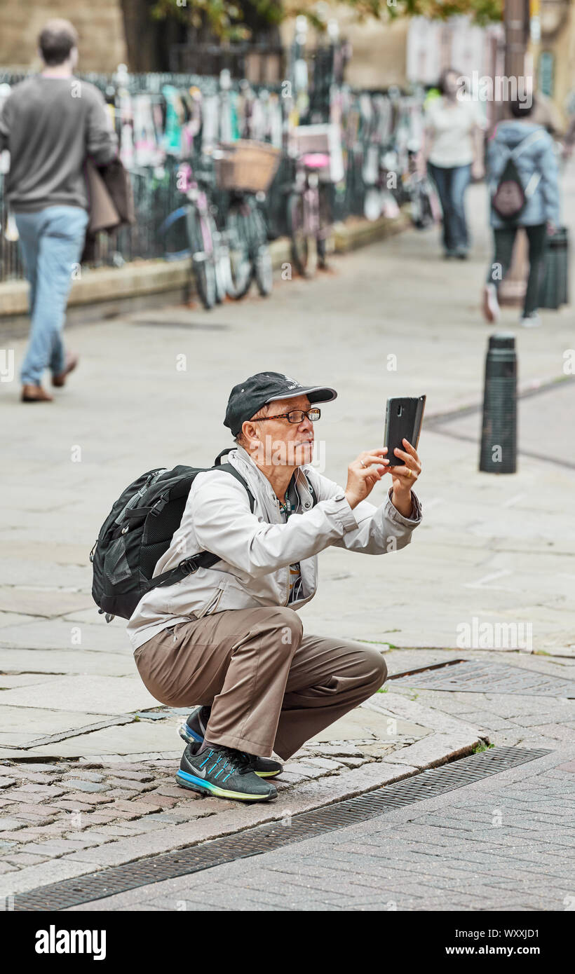 A chinese man squats and uses his camera to take a photo of St John's ...