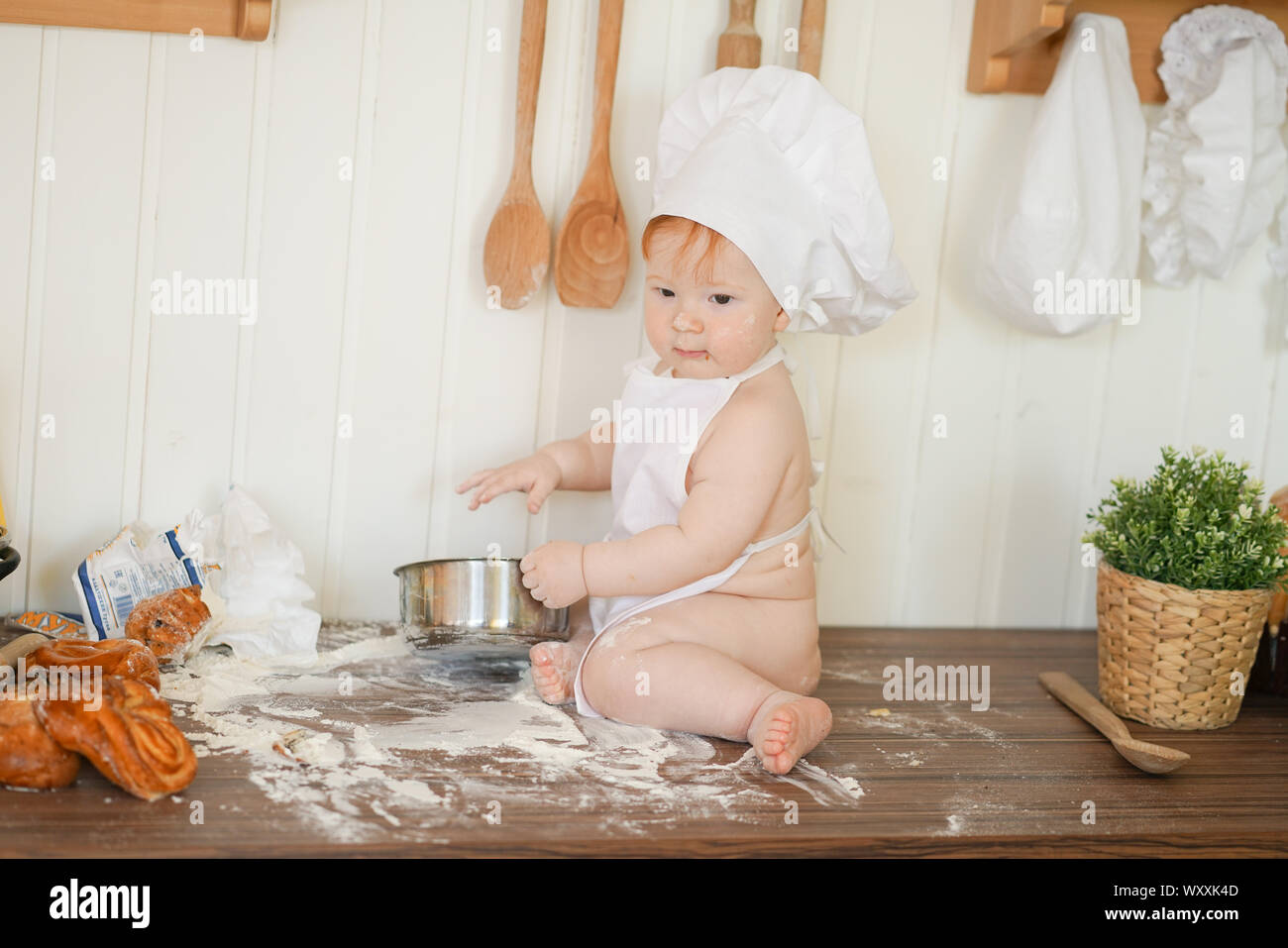 little baker child in chef hat at kitchen table alone with bread and ...