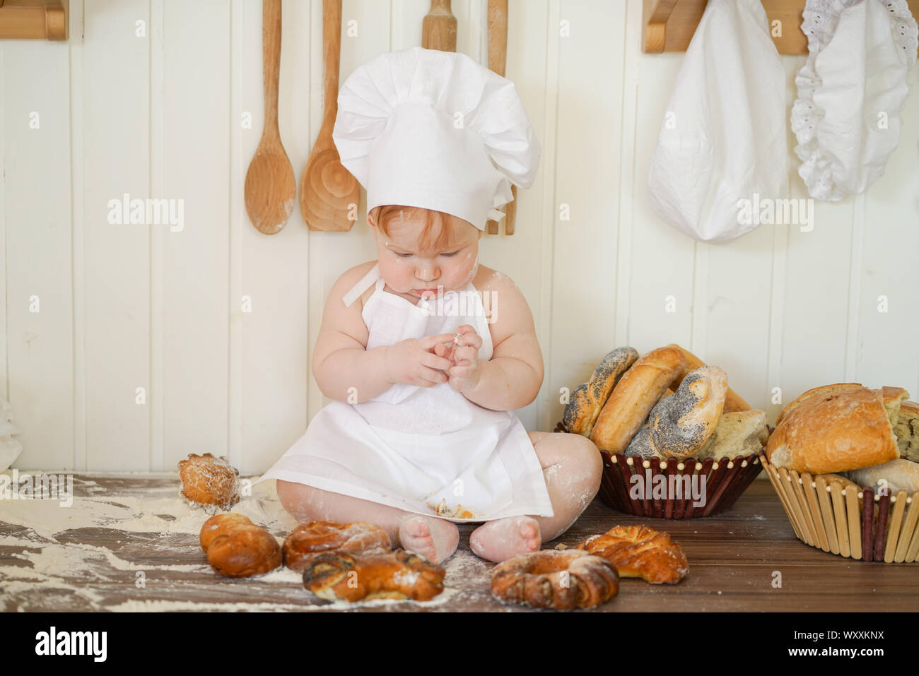 little baker child in chef hat at kitchen table alone with bread and ...