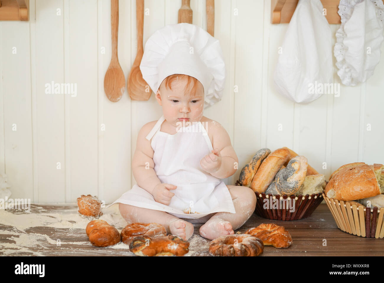 little baker child in chef hat at kitchen table alone with bread and ...