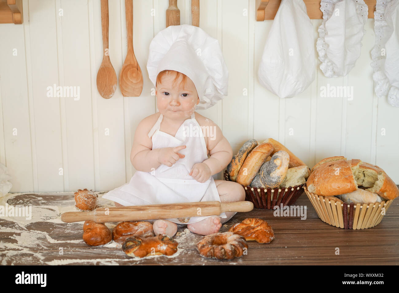 little baker child in chef hat at kitchen table alone with bread and ...
