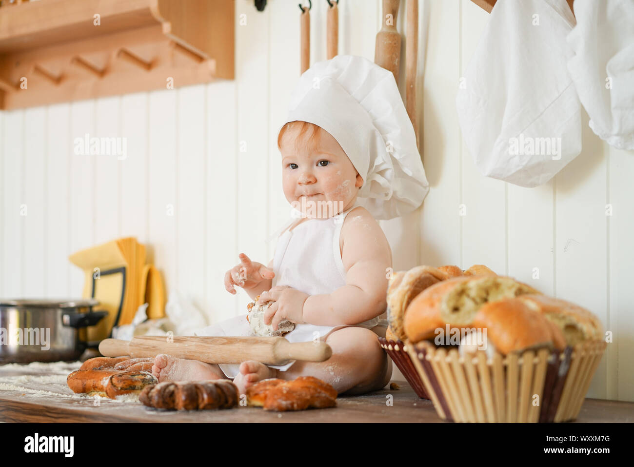 little baker child in chef hat at kitchen table alone with bread and ...