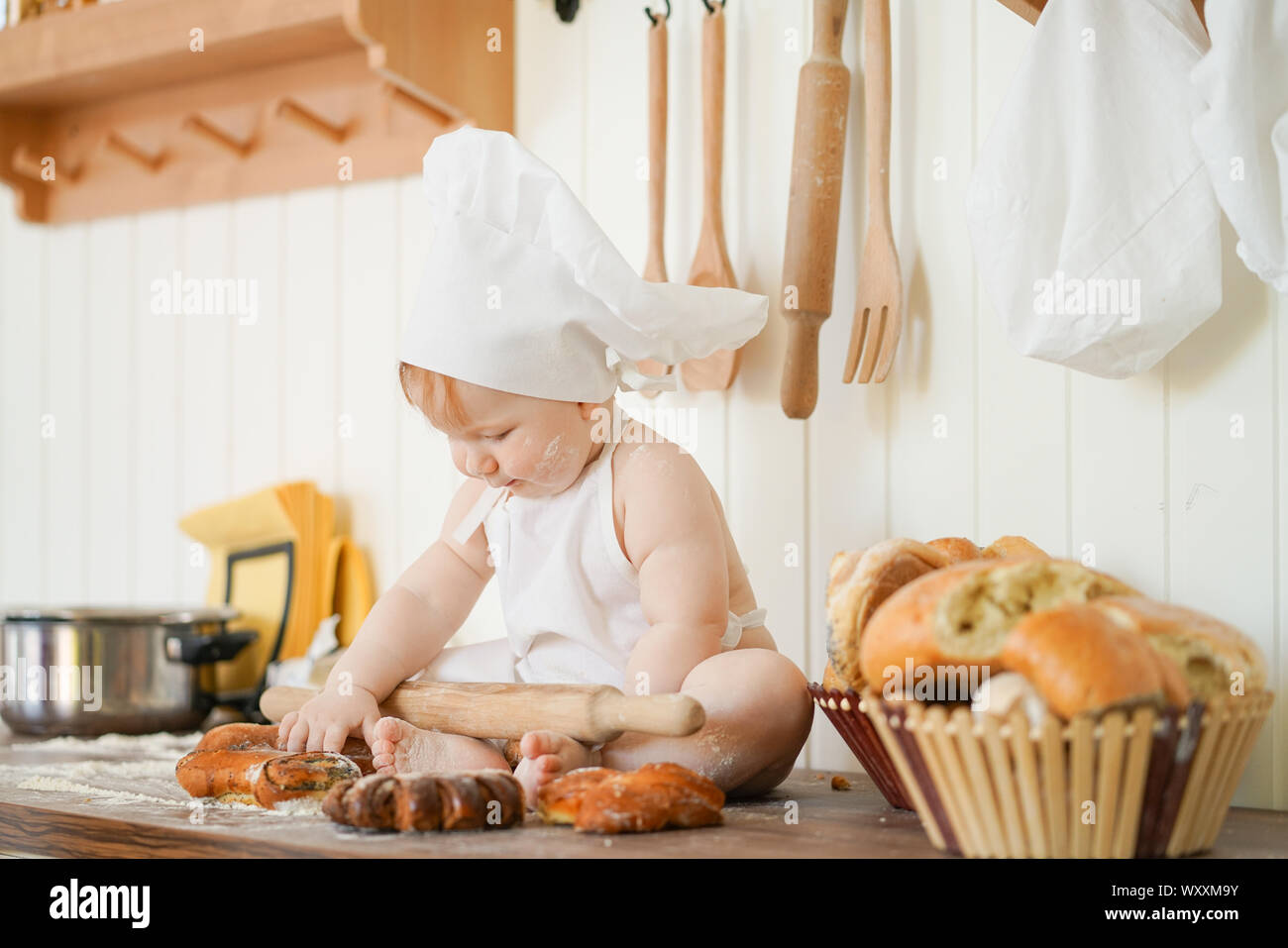 little baker child in chef hat at kitchen table alone with bread and ...