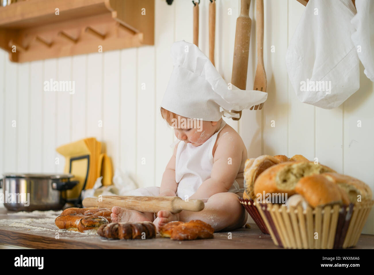 little baker child in chef hat at kitchen table alone with bread and ...