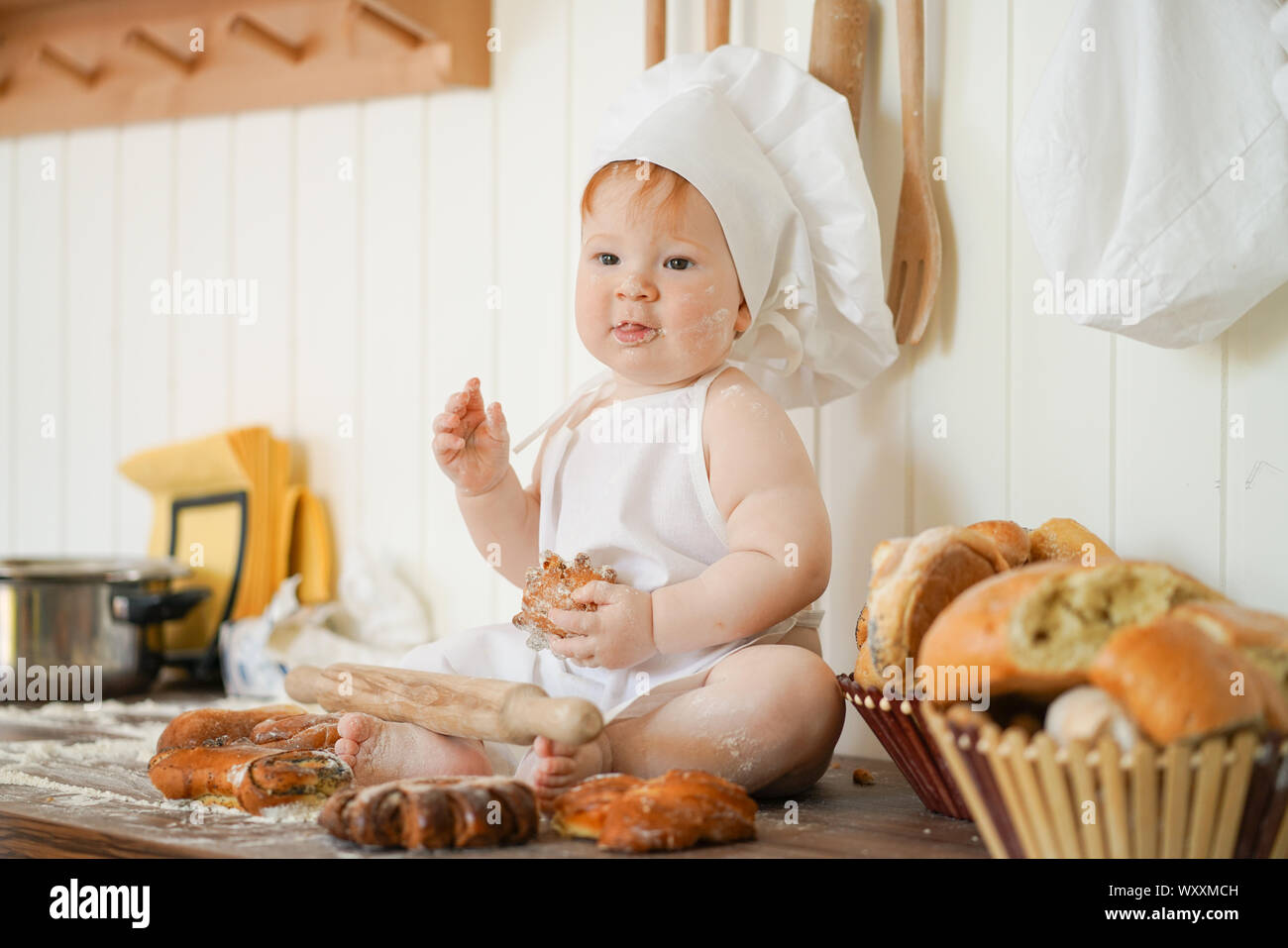 little baker child in chef hat at kitchen table alone with bread and ...