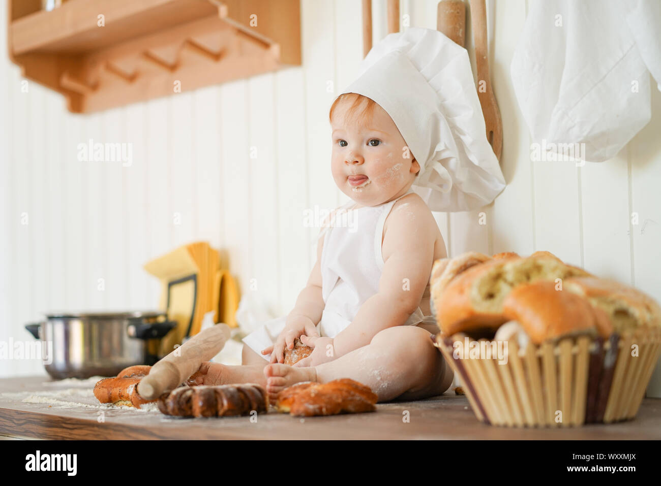 little baker child in chef hat at kitchen table alone with bread and ...