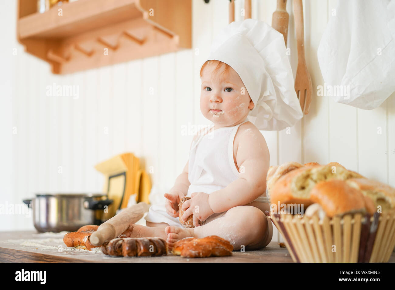 little baker child in chef hat at kitchen table alone with bread and ...
