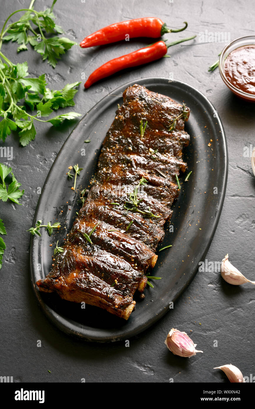 Grilled spare ribs on plate over black stone table. Tasty bbq meat. Top ...