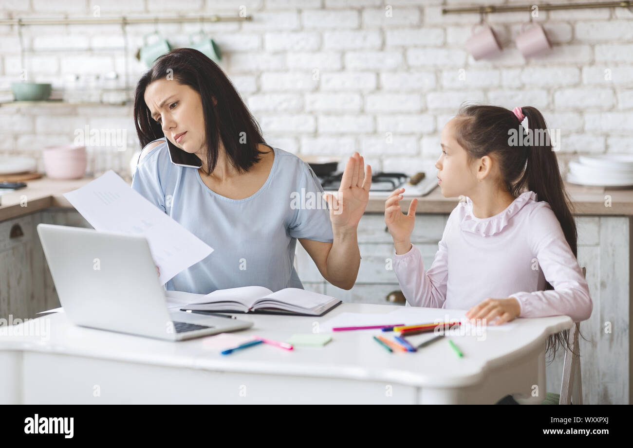 Busy mother frowning and turning away from daughter while working Stock ...