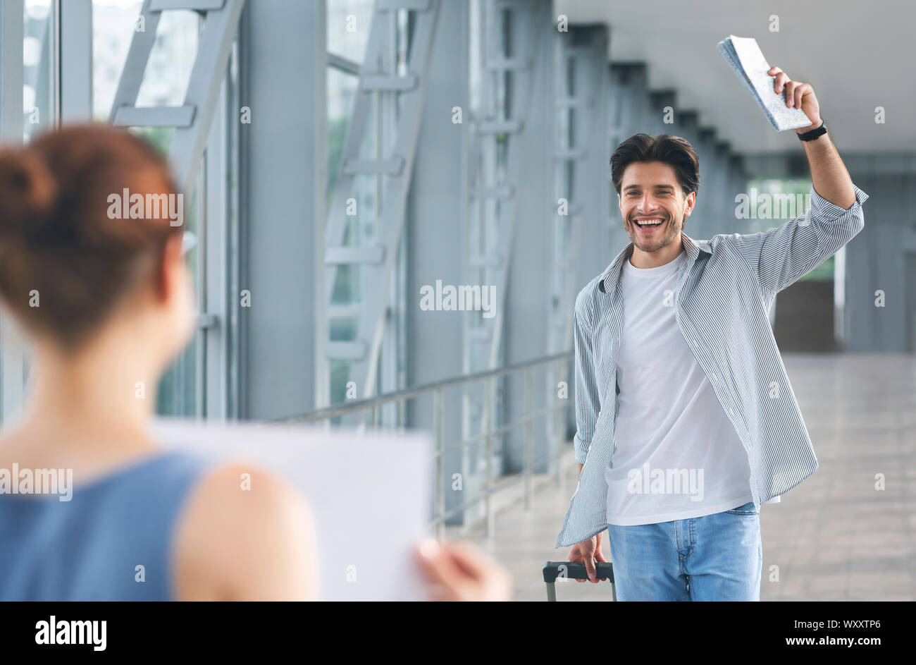 Passenger walking with luggage to woman with name board Stock Photo - Alamy