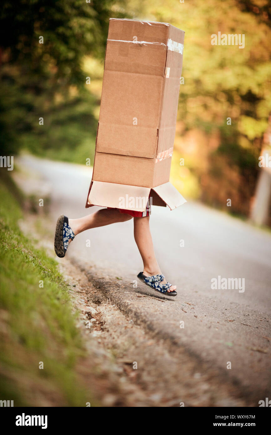 A small boy struggles to remove the box off his body while walking on ...