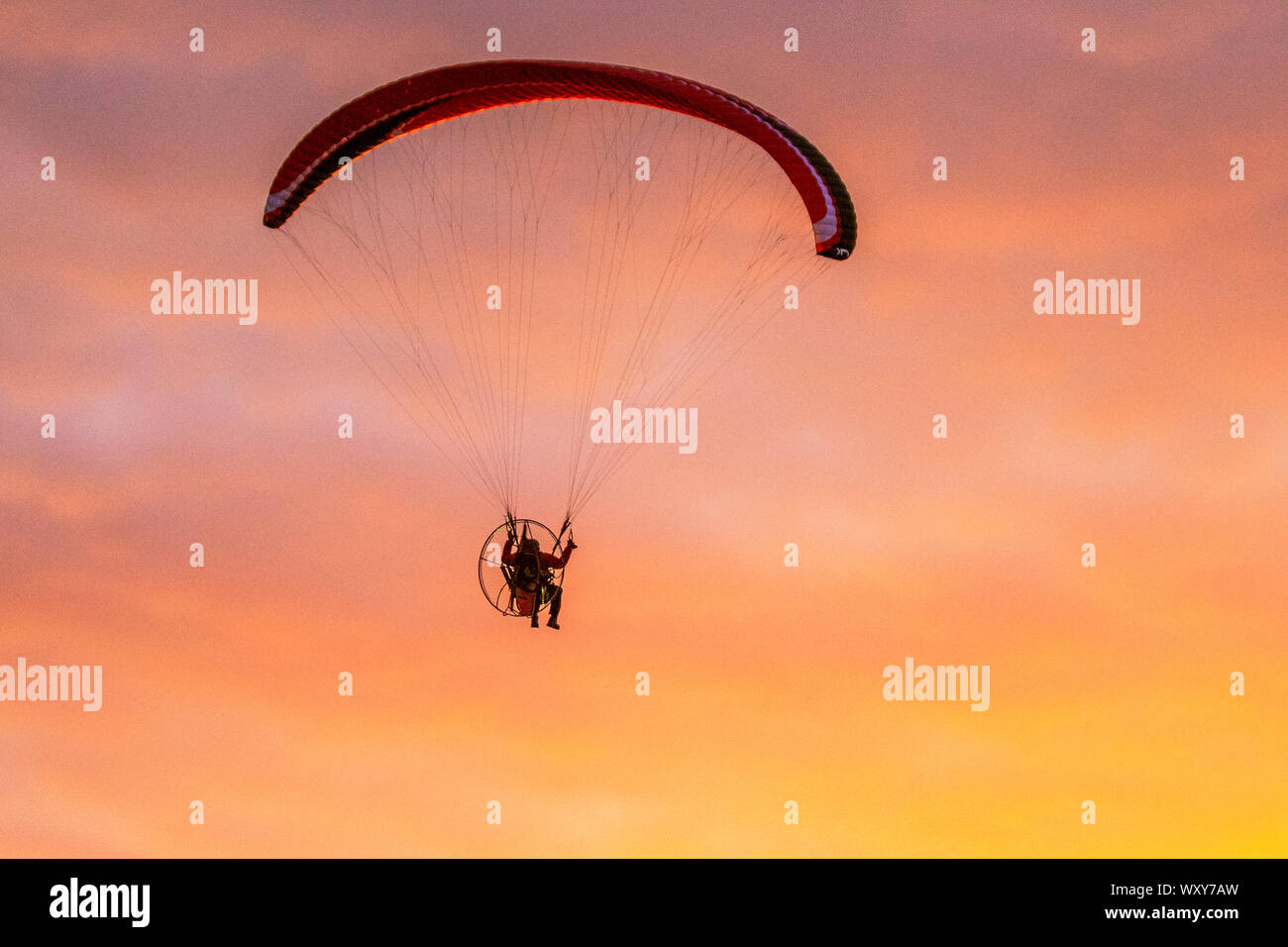 Powered hand glider silhouetted in the evening sun, takes a motorized ...