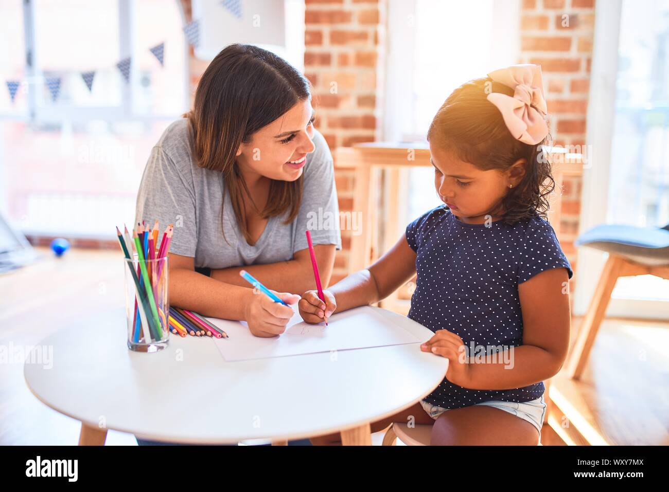 Beautiful teacher and toddler girl drawing draw using colored pencils ...