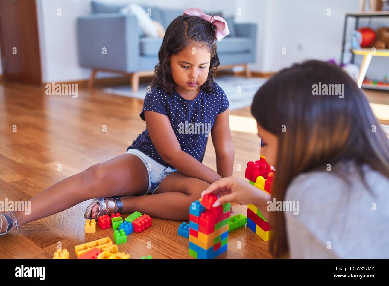 Beautiful teacher and toddler girl playing with construction blocks ...