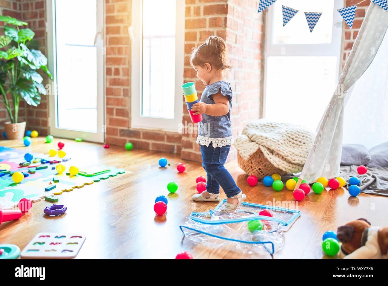 Beautiful toddler standing playing with colorful plastic cups at ...