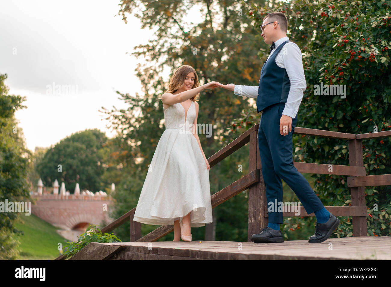 Wedding couple on stairs at park. Groom in blue suit giving hand to ...