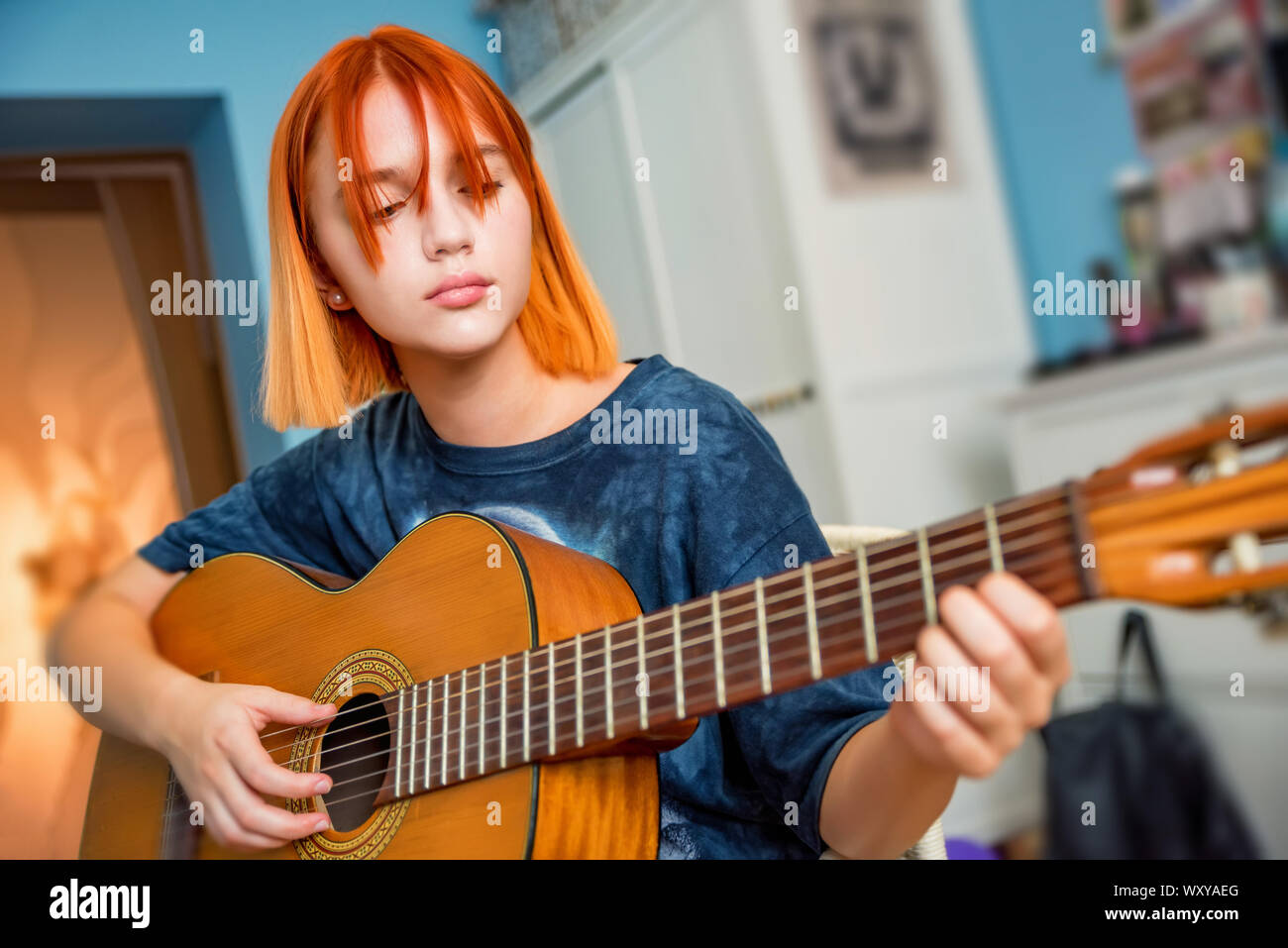 View of beautiful red-haired teen girl playing guitar in her bedroom ...