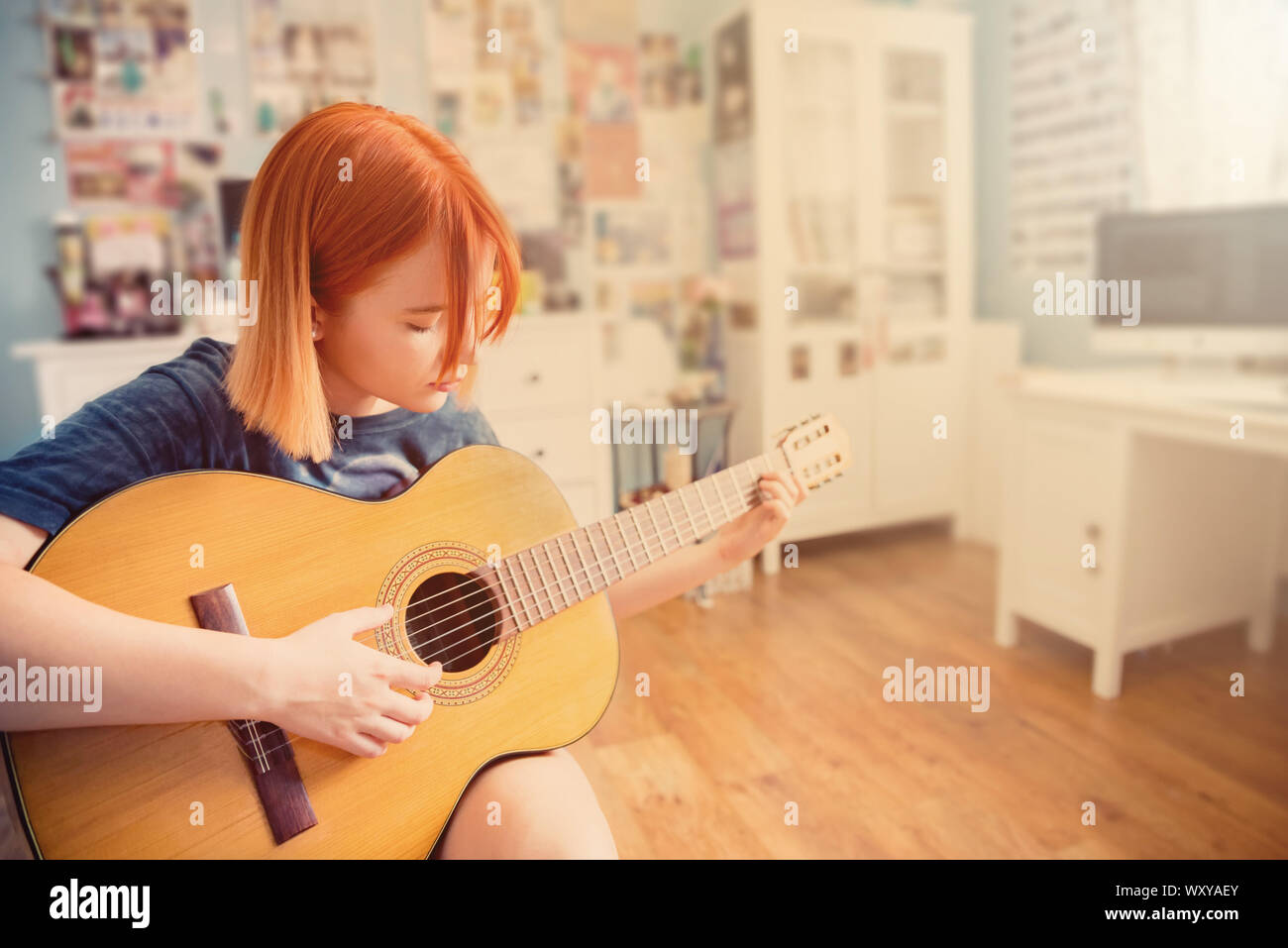 View of beautiful red-haired teen girl playing guitar in her bedroom ...