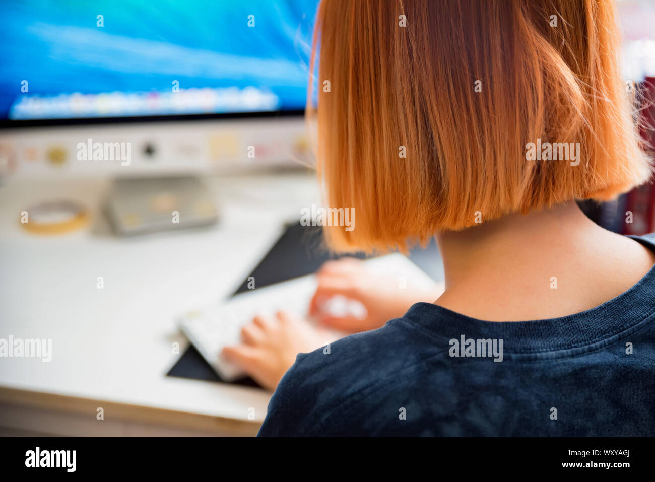 Back view of beautiful red-haired teen girl typing something on ...