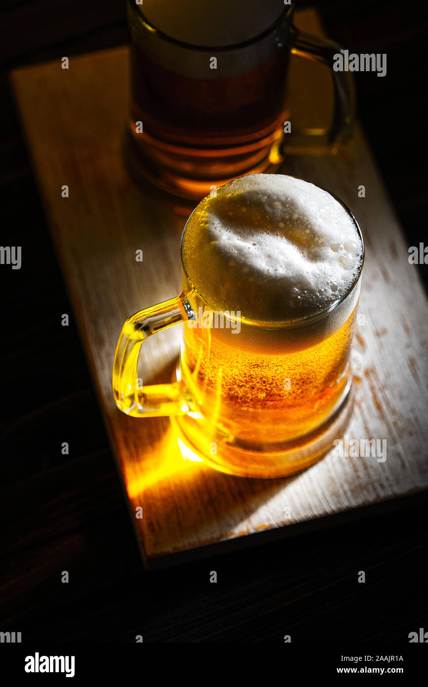 Zwei helle Bier Becher mit weißer Schaum auf dunklen Holztisch. Ansicht ...