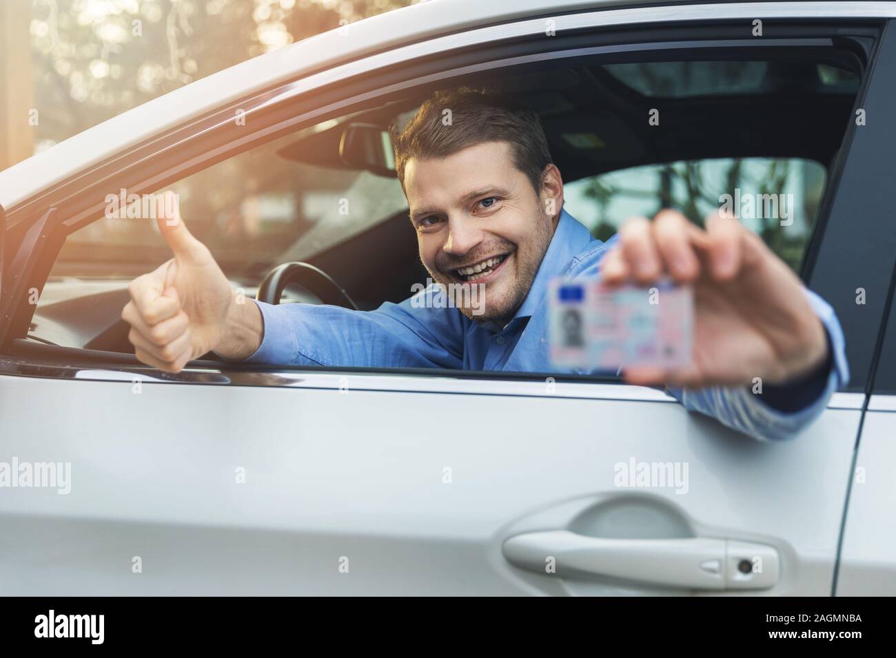 Junge lächelnde Mann sitzt im Auto und zeigt seine neuen Führerschein ...