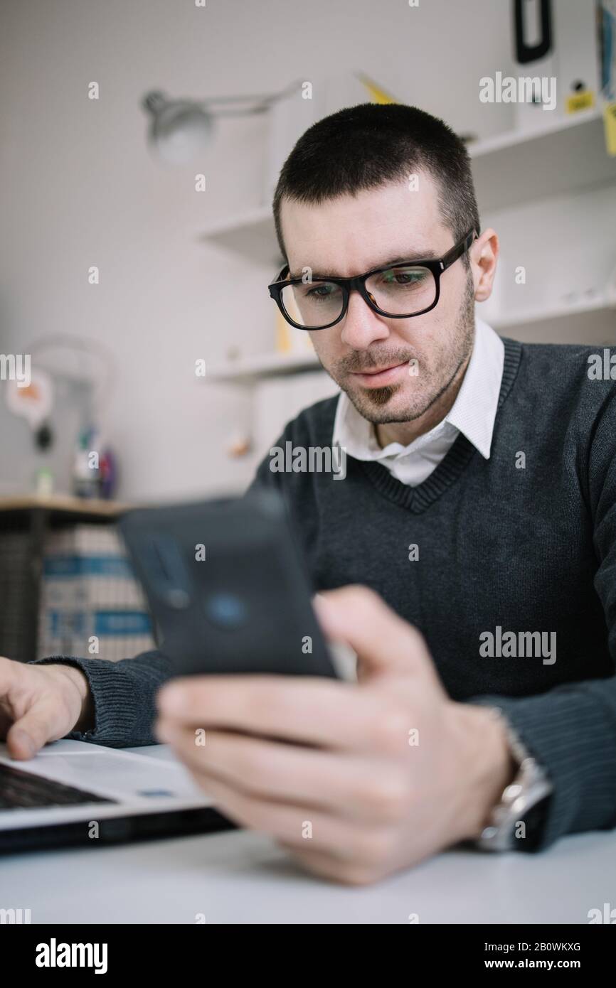 Junger Mann mit Brille, der auf sein Telefon blickt. Ein Geschäftsmann ...