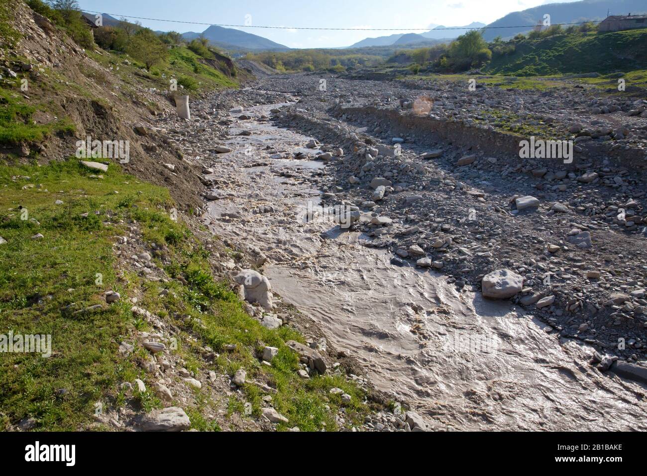 Steiniger Fluss, hohe grüne Berge im Hintergrund. Felsen auf Flussbett ...