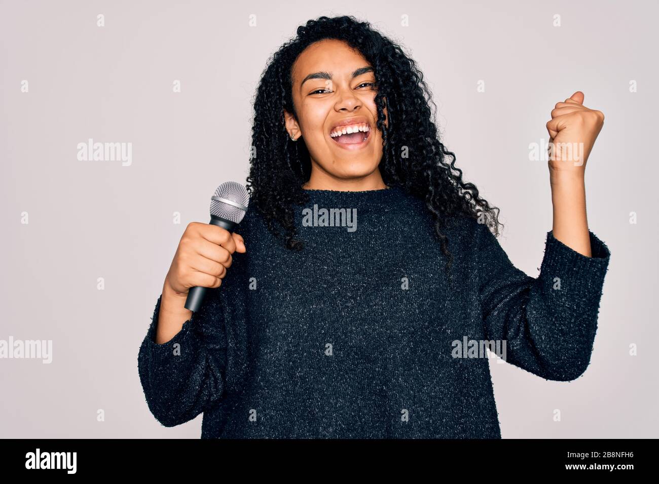 Junge afroamerikanische Curly Singer-Frau, die mit Mikrofon über weißem ...