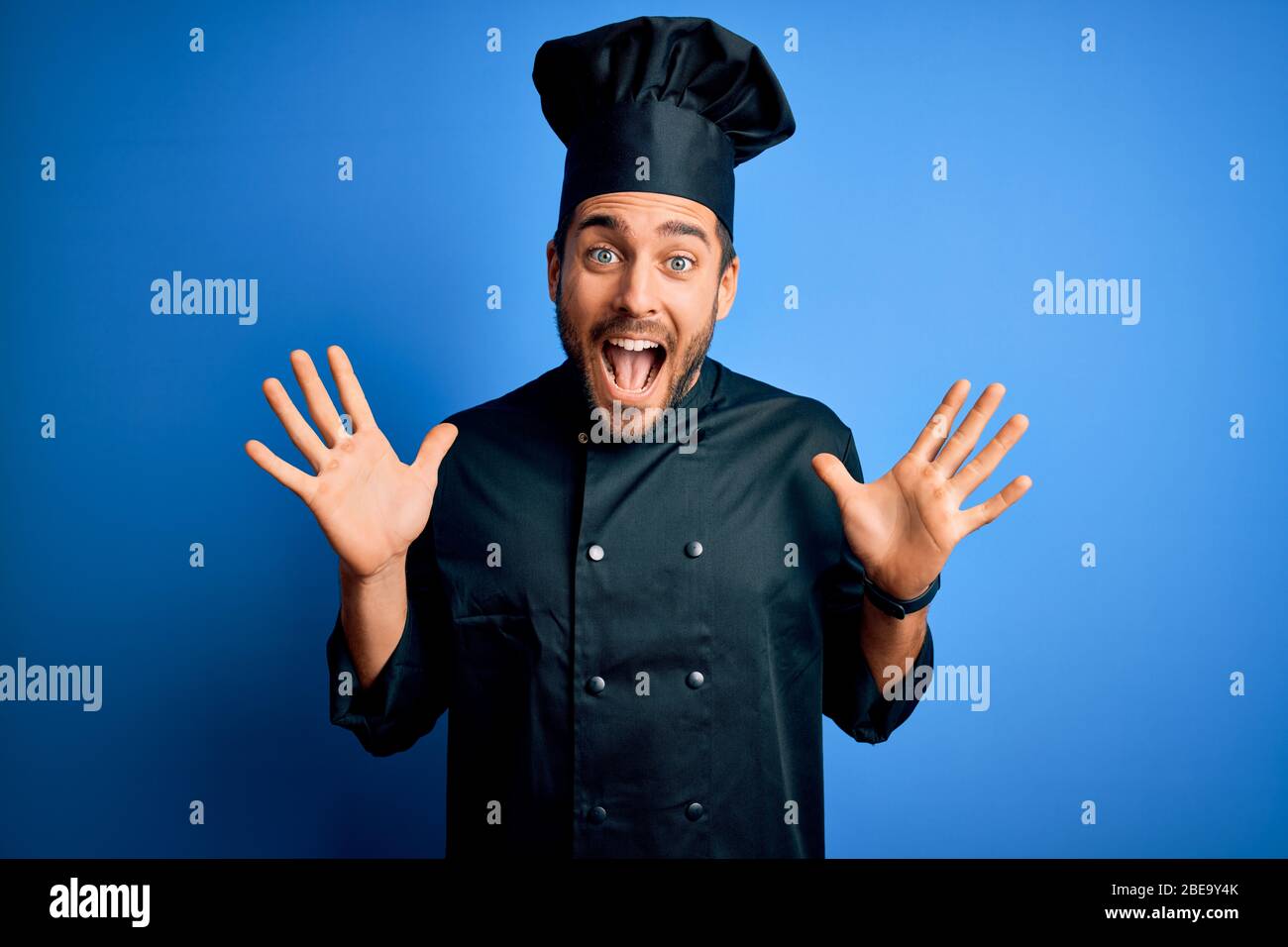 Junge gutaussehende Koch Mann mit Bart trägt Kocher Uniform und Hut ...