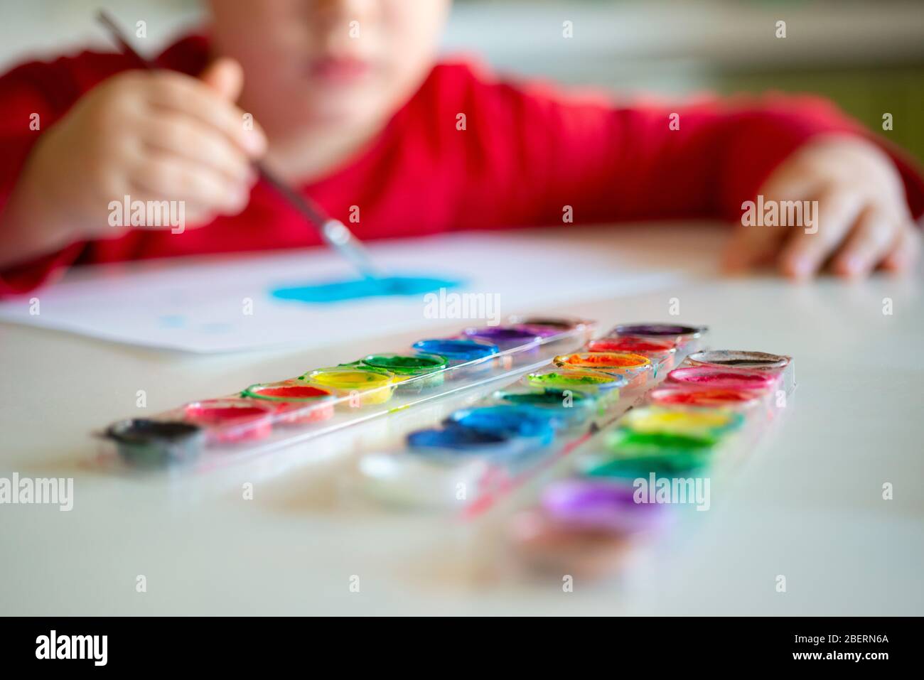 Der Junge lernt, mit einem Pinsel auf Papier zu malen, der an einem ...