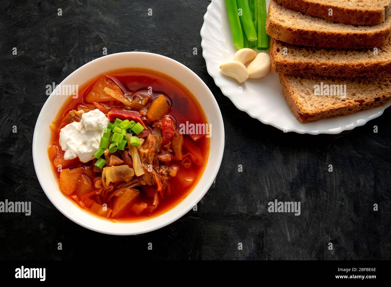 Borscht-Suppe in einer weißen Schüssel mit schwarzem Brot, grüner ...
