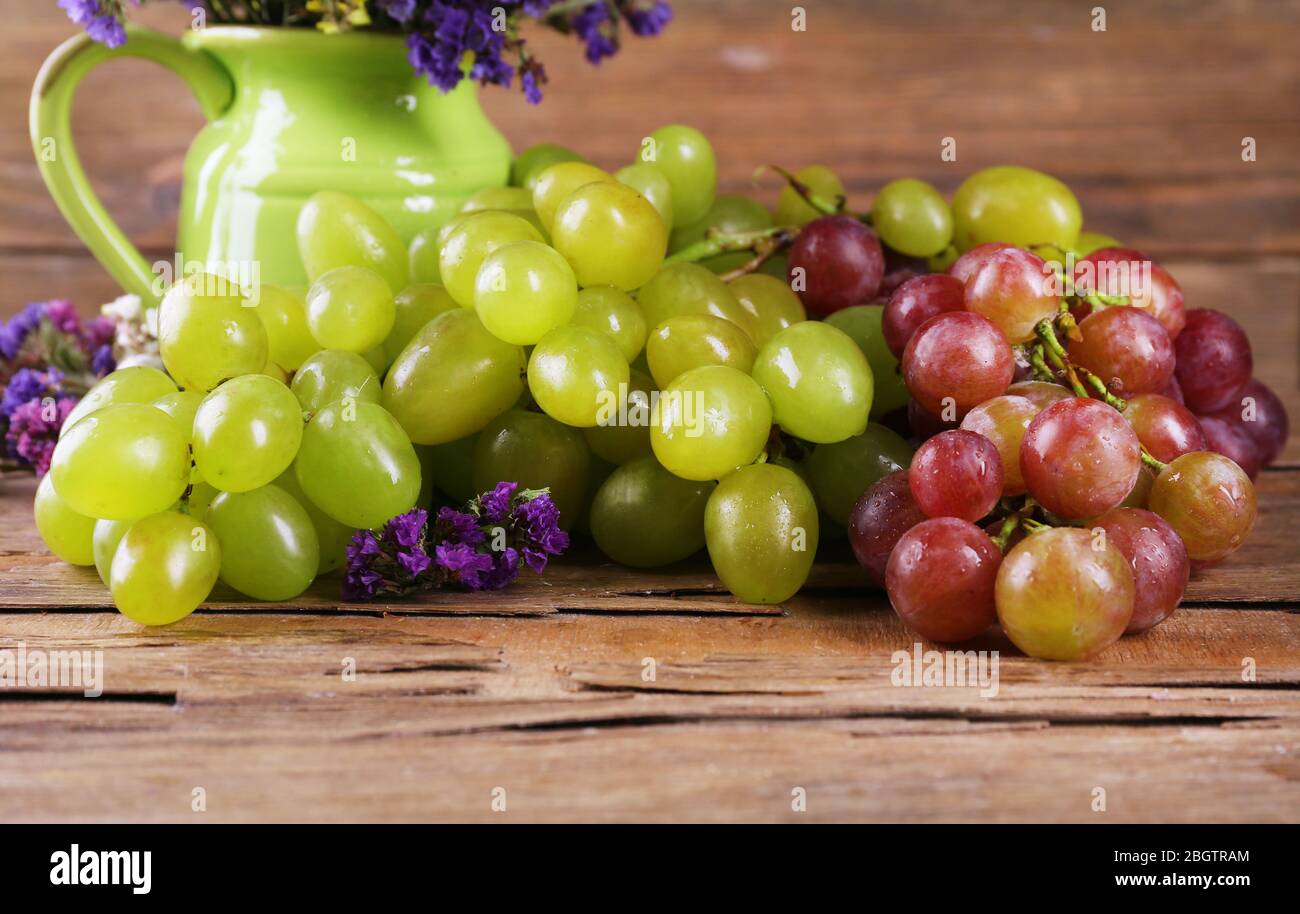 Trauben von reifen Trauben und Vase mit frischen Blumen auf Holztisch ...