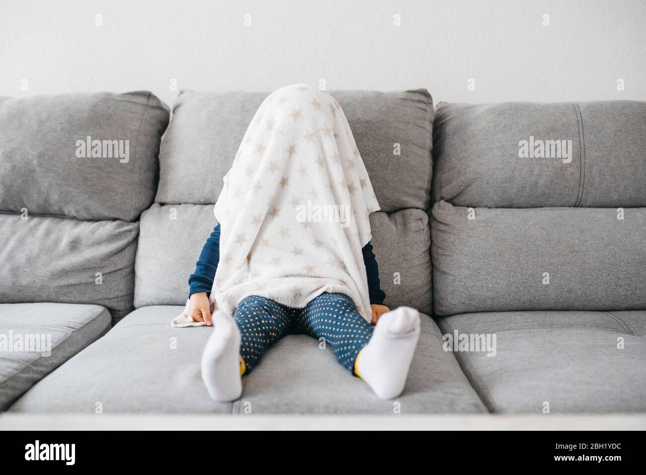 Kleines Mädchen, das zu Hause auf der Couch sitzt und sich unter der ...