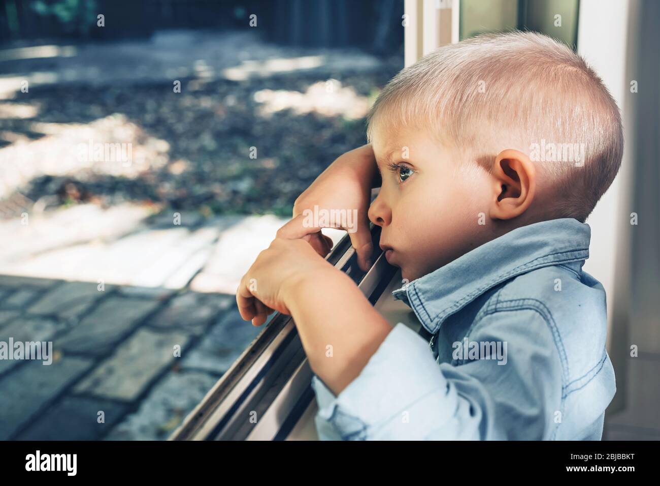 Kleiner Junge, der durch offenes Fenster nach draußen schaut. Bleiben ...