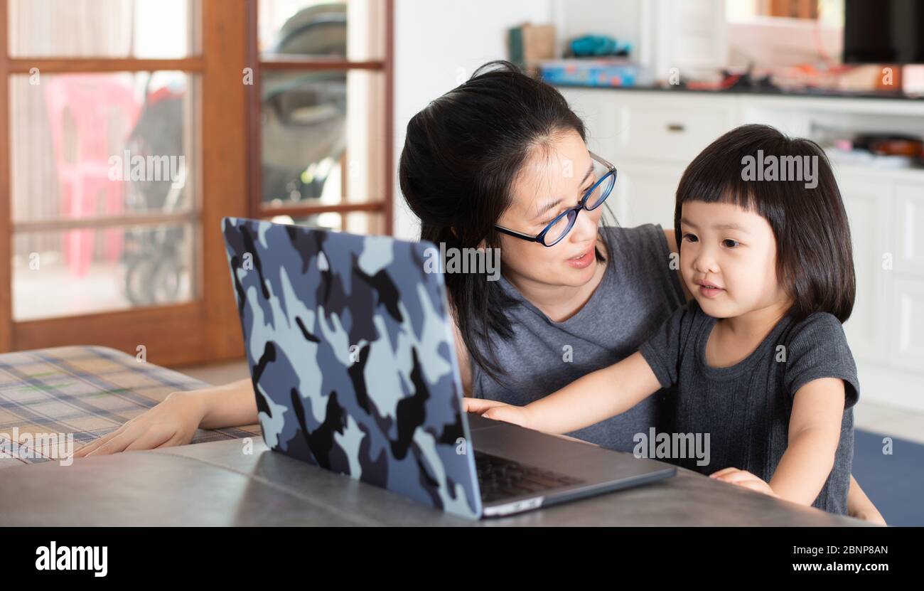 Ein asiatisches Mädchen lernt mit ihrer Mutter Online-Unterricht von einem Notebook-Computer ...