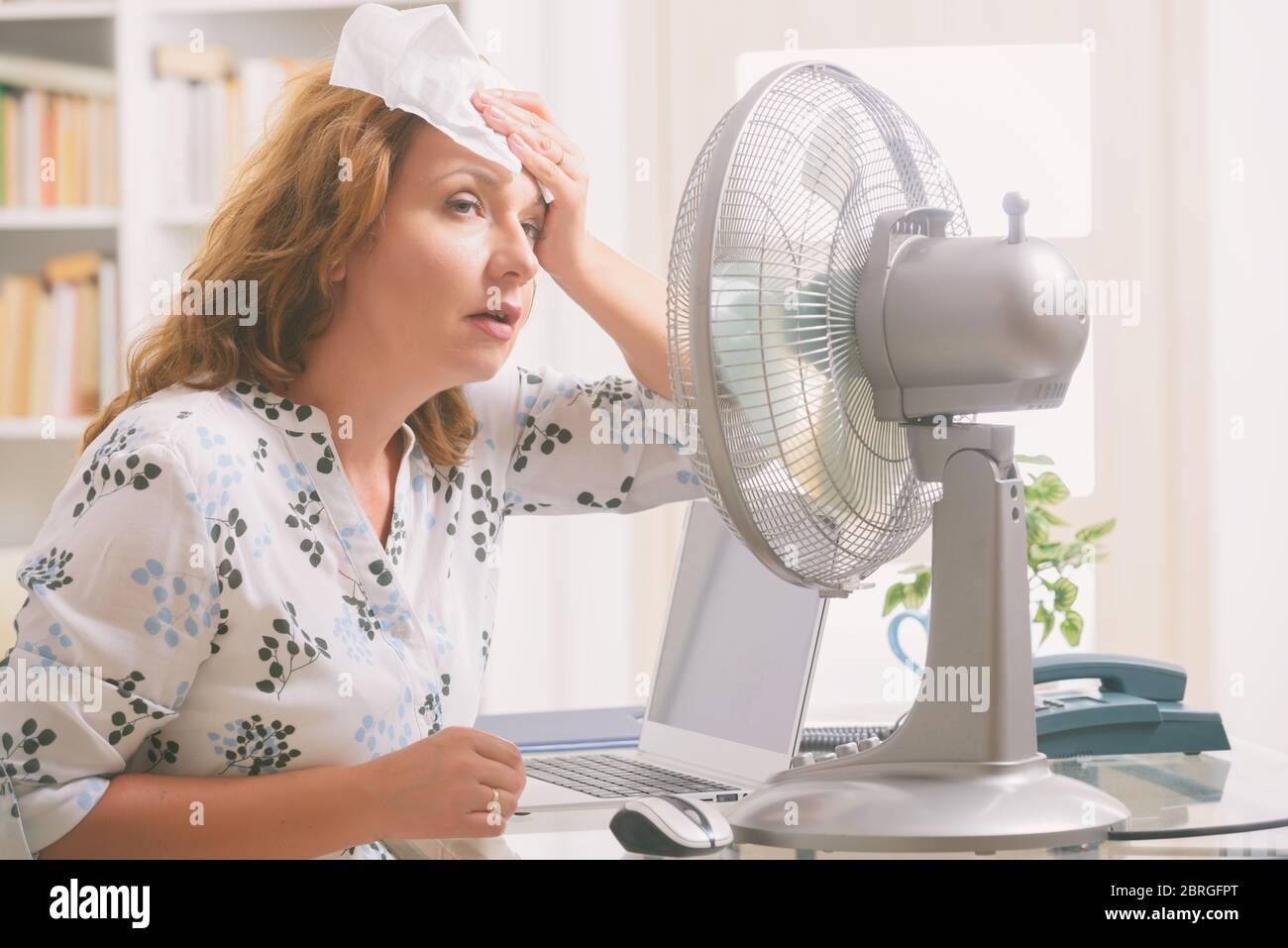 Frau leidet unter der Hitze, während der Arbeit im Büro und versucht ...