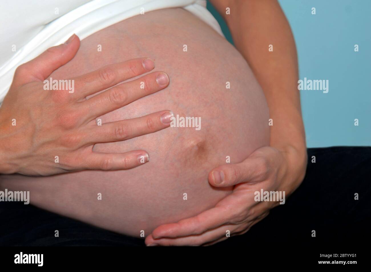 Mutter legt ihre Hände auf ihren vergrößerten Bauch. Die eine Hand ist ...