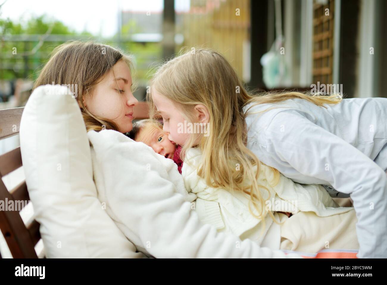 Zwei große Schwestern bewundern ihren neugeborenen Bruder. Zwei junge Mädchen halten ihren neuen ...
