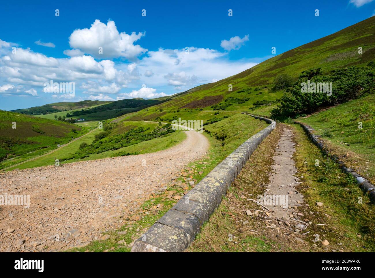 Schotterweg, der ins Tal führt mit altem Staudamm, dem Wasserlauf ...