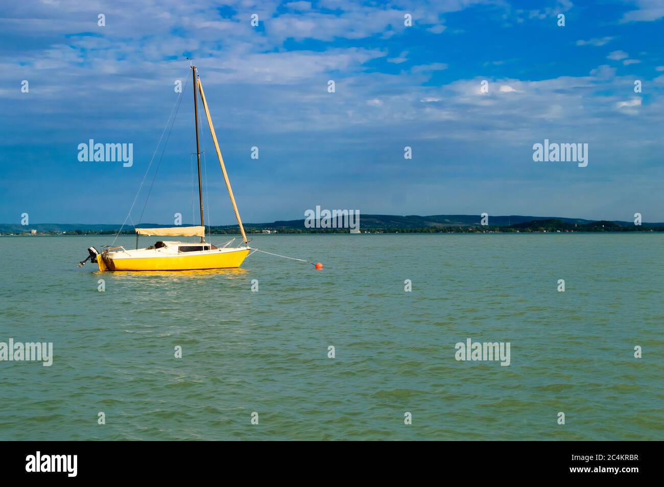 Ein gelbes Segelboot, das bei leicht bewölktem Wetter auf dem Wasser ...