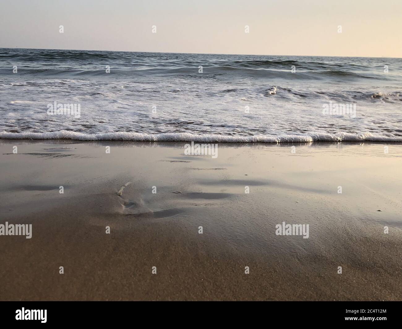 Das wellige Meer trifft auf den Sandstrand und glänzt unter dem Farbenfroher Himmel ...