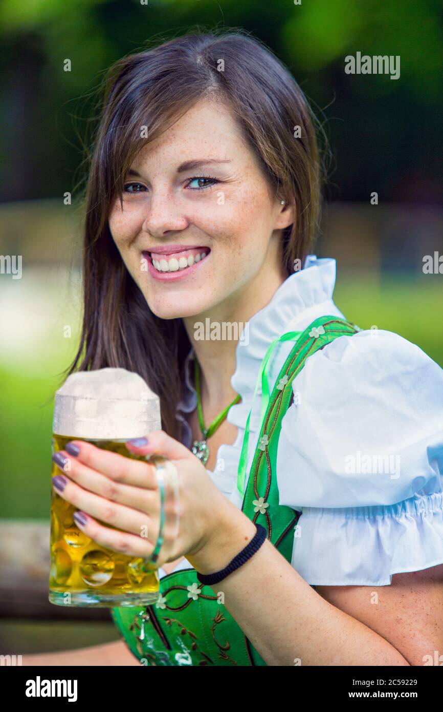 Junge Brünette Frau in bayrischen Dirndl mit einem Becher mit Bier ...