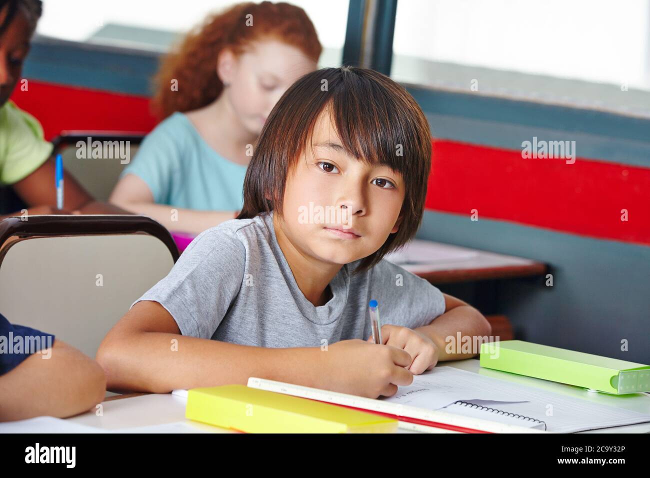 Japanischer Junge sitzt in einer Grundschule Klassenzimmer und schreibt ... Japanischer Junge sitzt in einer Grundschule Klassenzimmer und schreibt ...