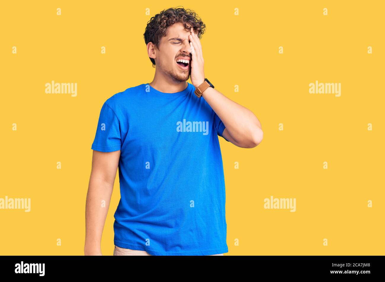 Junger hübscher Mann mit lockigem Haar trägt lässige Kleidung gähnend ...