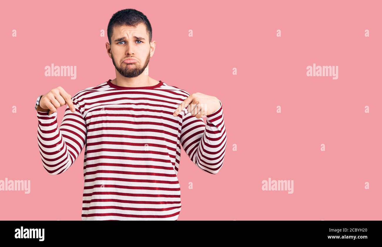 Junger, hübscher Mann mit gestreiftem Pullover, der traurig und ... Junger, hübscher Mann mit gestreiftem Pullover, der traurig und ...