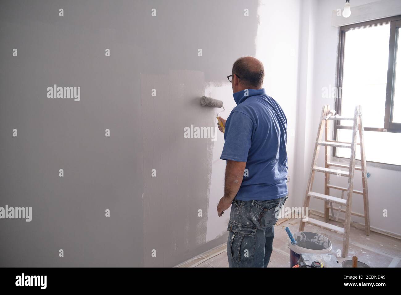 Echter Seniorenmaler malt eine graue Wand mit einer Malerrolle. Echt ...