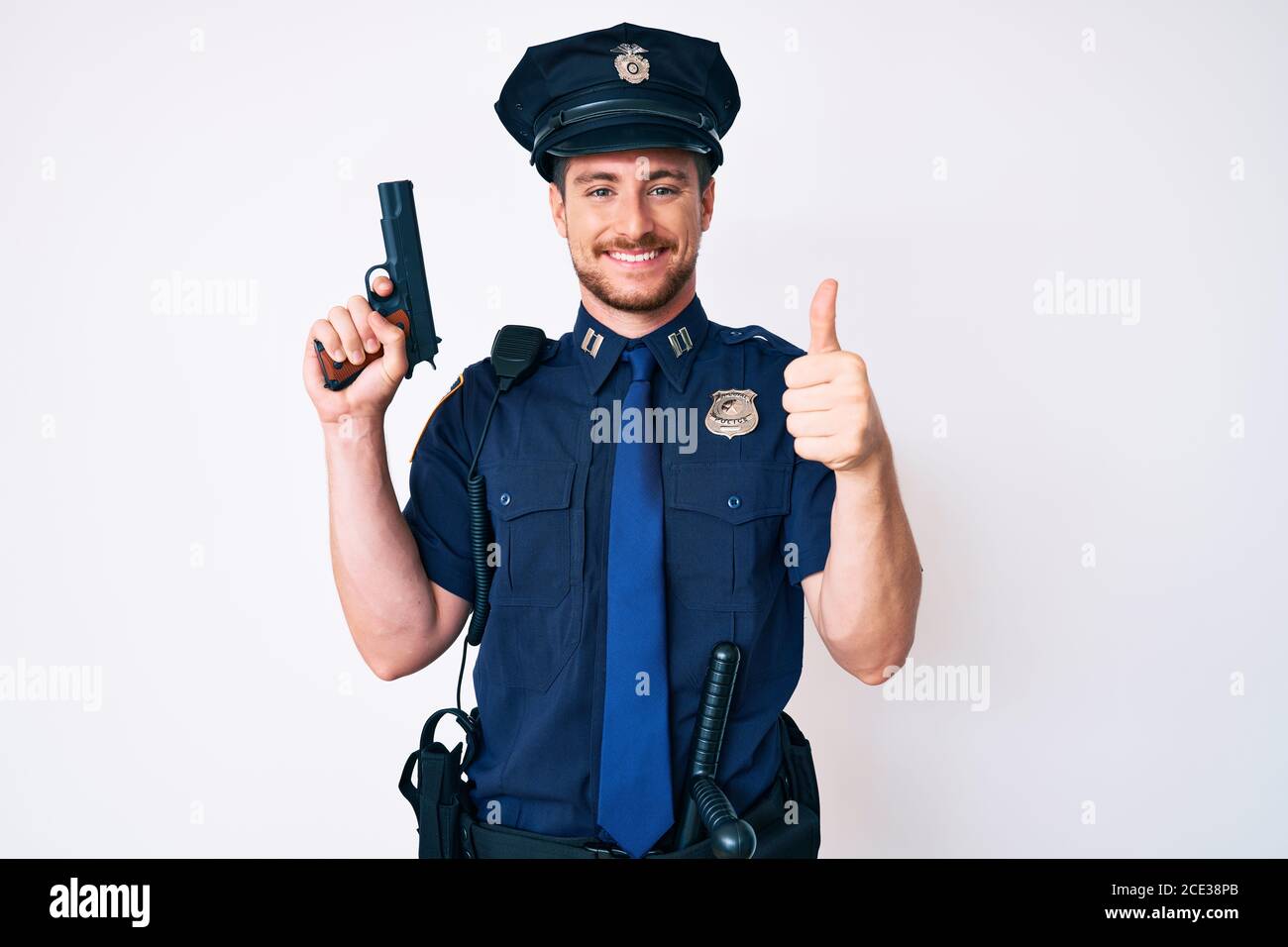 Junger kaukasischer Mann in Polizeiuniform, der die Waffe hält, lächelt ...